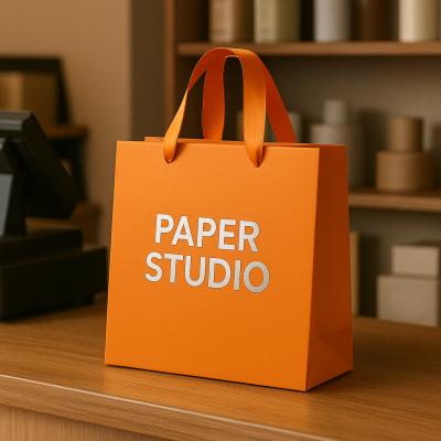 China Luxury Eco-Friendly Custom Logo Printing Silk Ribbon Handles Orange Paperboard Shopping Bags For Gift Clothing Boutique for sale
