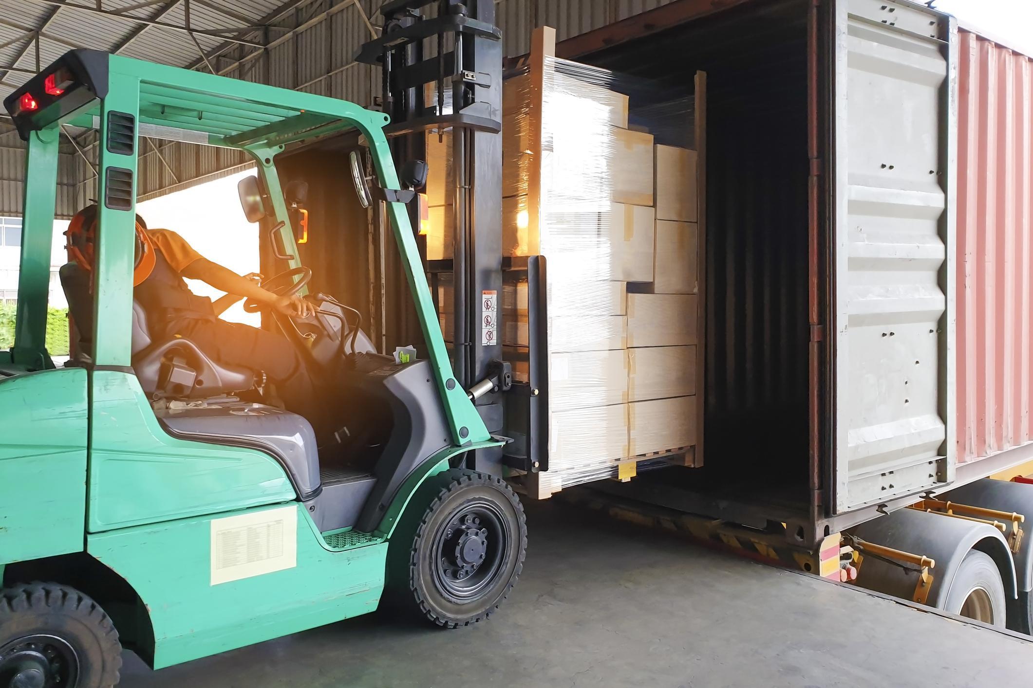 Forklift driver loading goods pallet into the truck container, freight industry warehouse logistics and transport