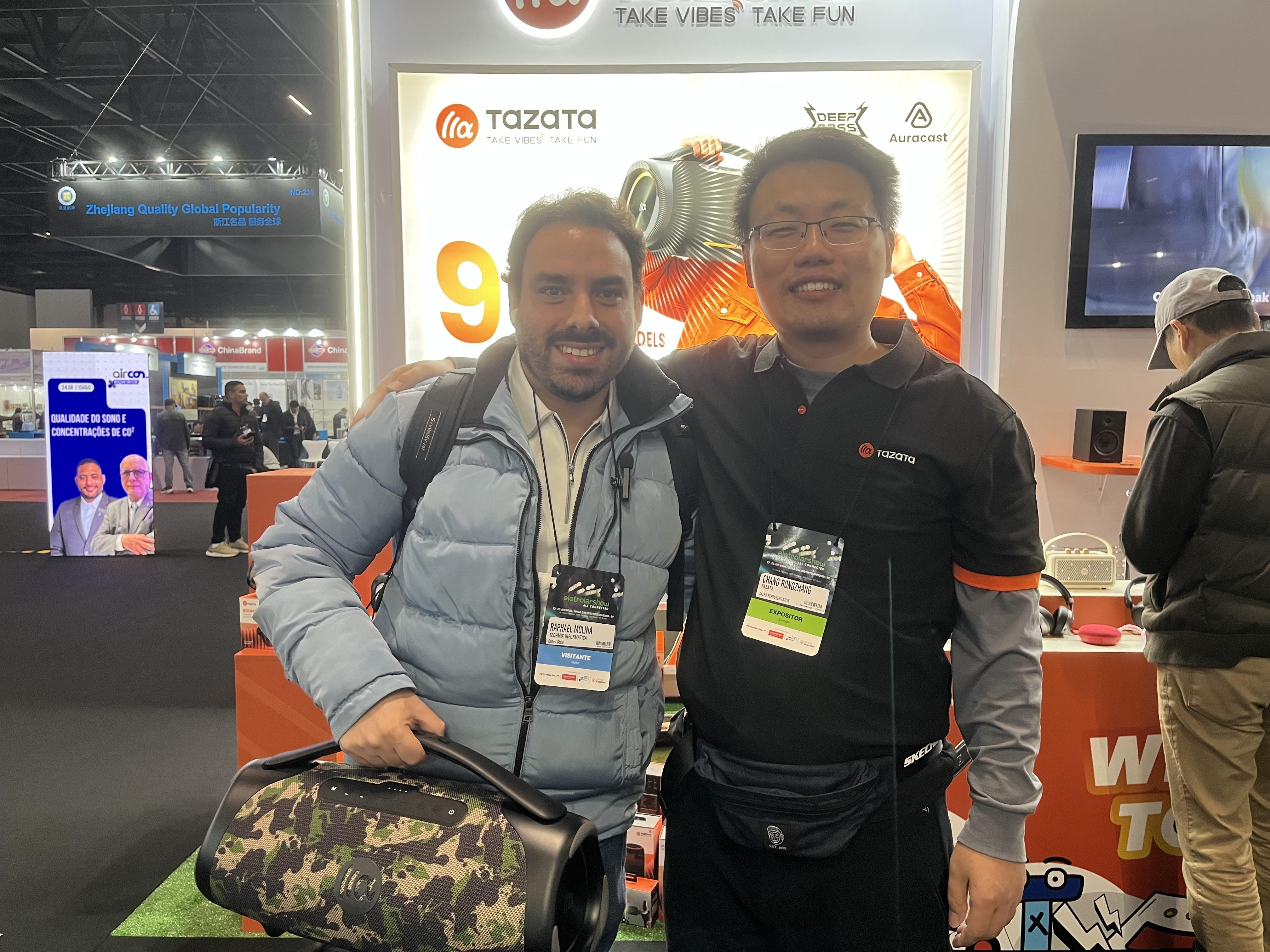 A delighted Brazilian client proudly holding their newly purchased TAZATA Audio sample speaker, sharing an authentic, joyful smile with the team at the ELETROLAR SHOW booth.