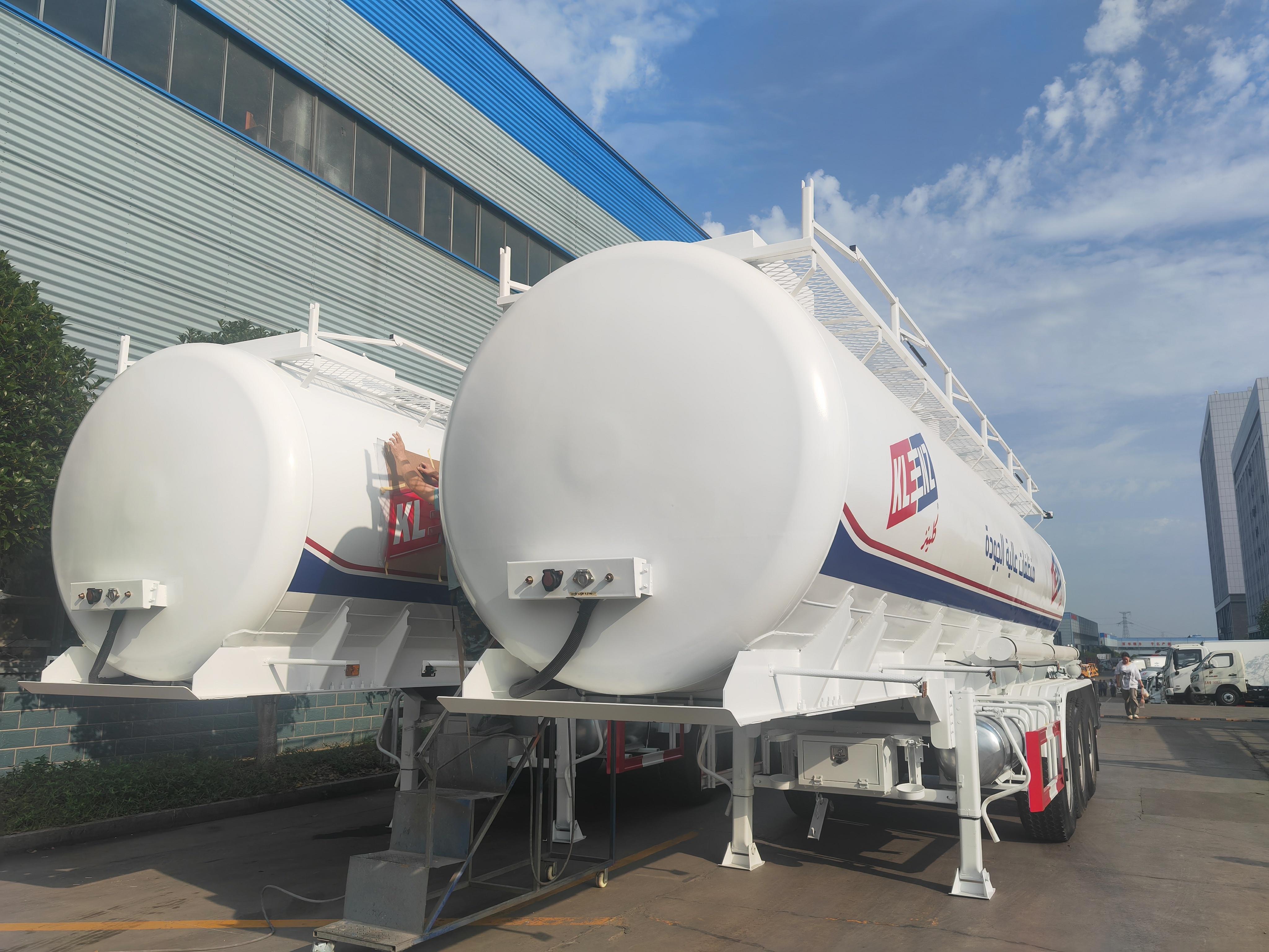 Front view of customized tri-axle liquid cleanser tanker trailer showing heavy-duty landing gear and worker adjusting the KLEENZ brand logo at CLW Group factory
