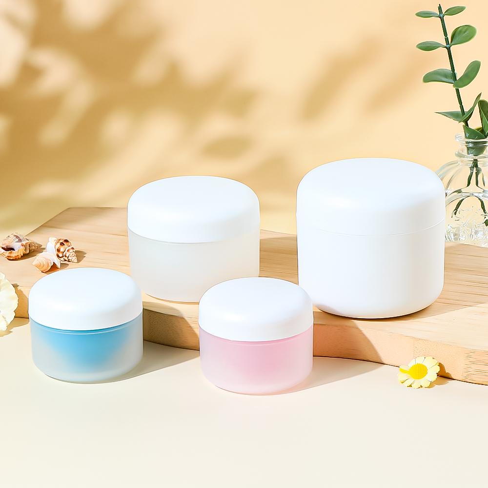 Round PP cream jars in white, pink and blue displayed on wooden tray.