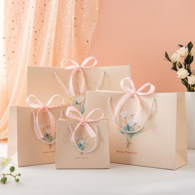 China Gift Bag Collection Premium Bow Tied Pastel Beige With Pink Bows Floral Design Hand Carry Paper Bags for sale