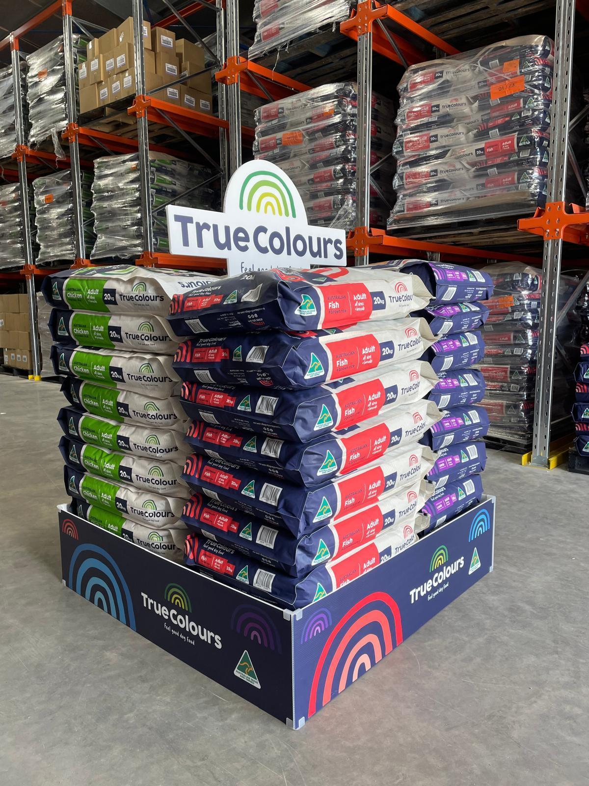 Warehouse pallet display of stacked 20kg eight side seal dog food pouches in chicken, fish and lamb flavors, custom branded retail pet food packaging bulk display for wholesale pet supply stores.