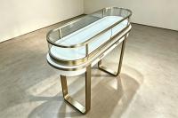 China Custom Luxury Oval Curved Glass Jewelry Display Table with Brushed Gold Metal Leg and Lockable Storage Drawer for sale