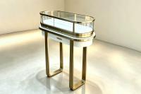 China Custom Luxury Oval Curved Glass Jewelry Display Table with Brushed Gold Metal Leg and Lockable Storage Drawer for sale