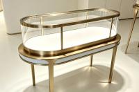 China Oval Curved Glass Jewelry Display Table with Slim Brushed Gold Metal Legs and Built-in LED Lighting for sale